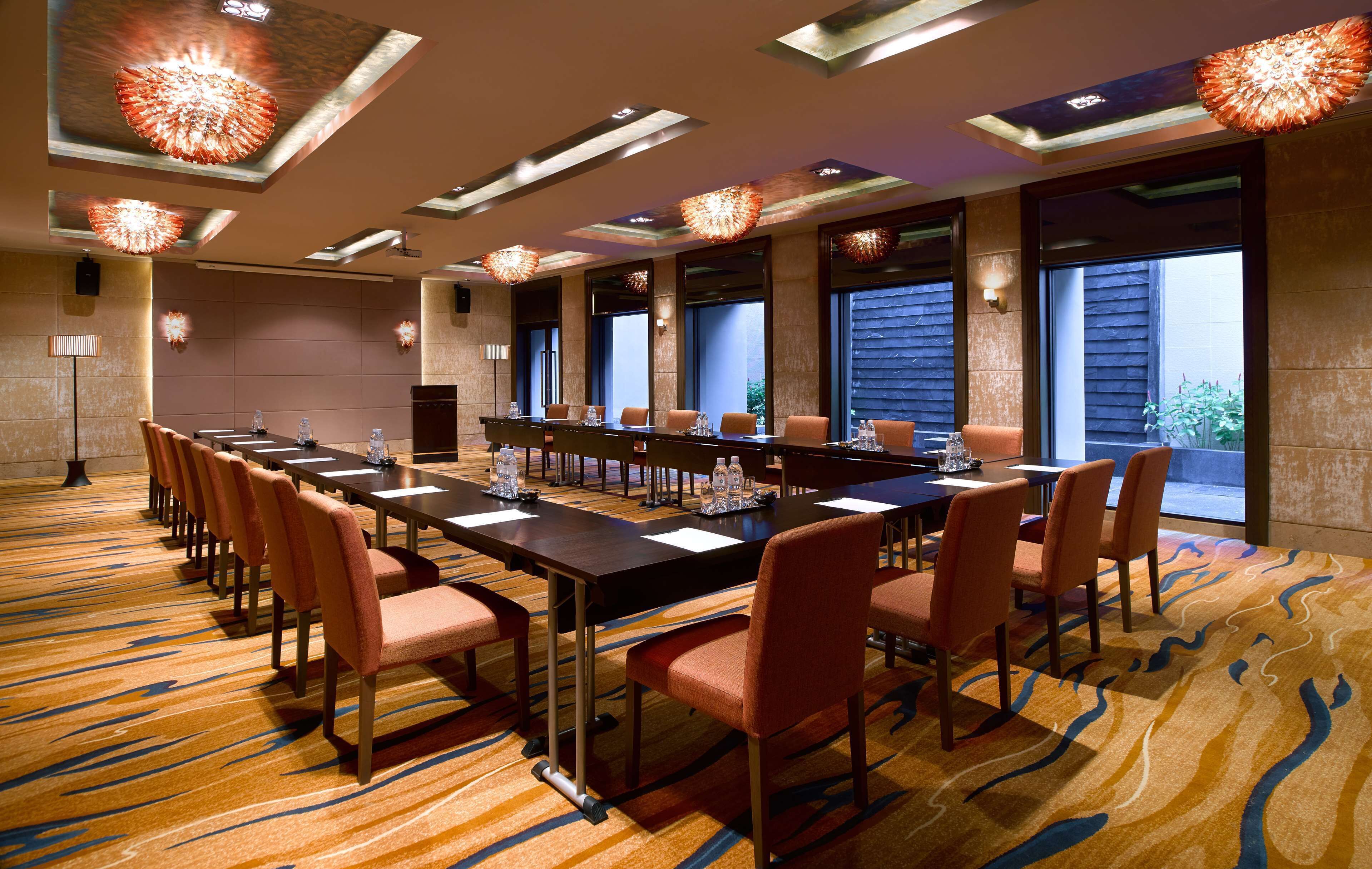 Uma sala de conferências com uma mesa comprida, várias cadeiras e janelas amplas.