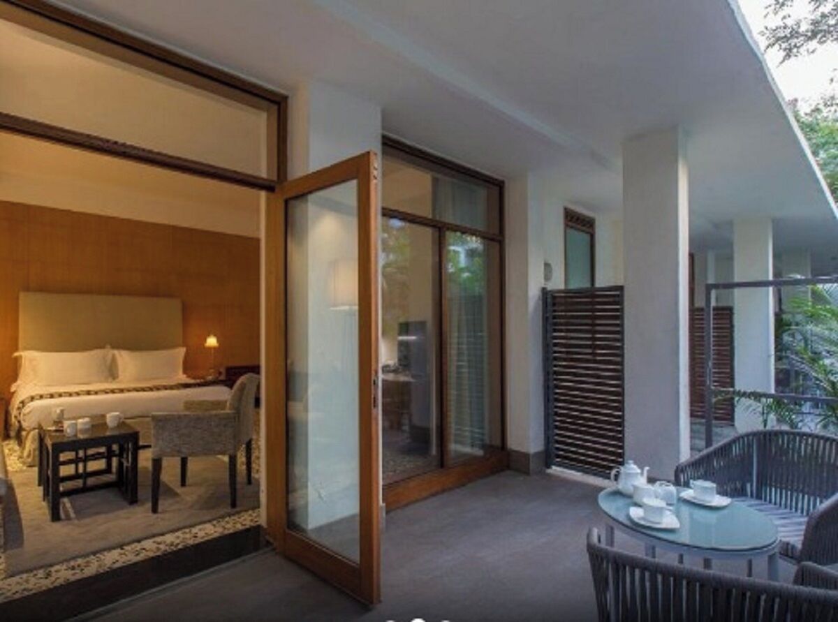 Quarto de hotel com uma cama, uma mesinha e uma varanda com mesa e cadeiras.