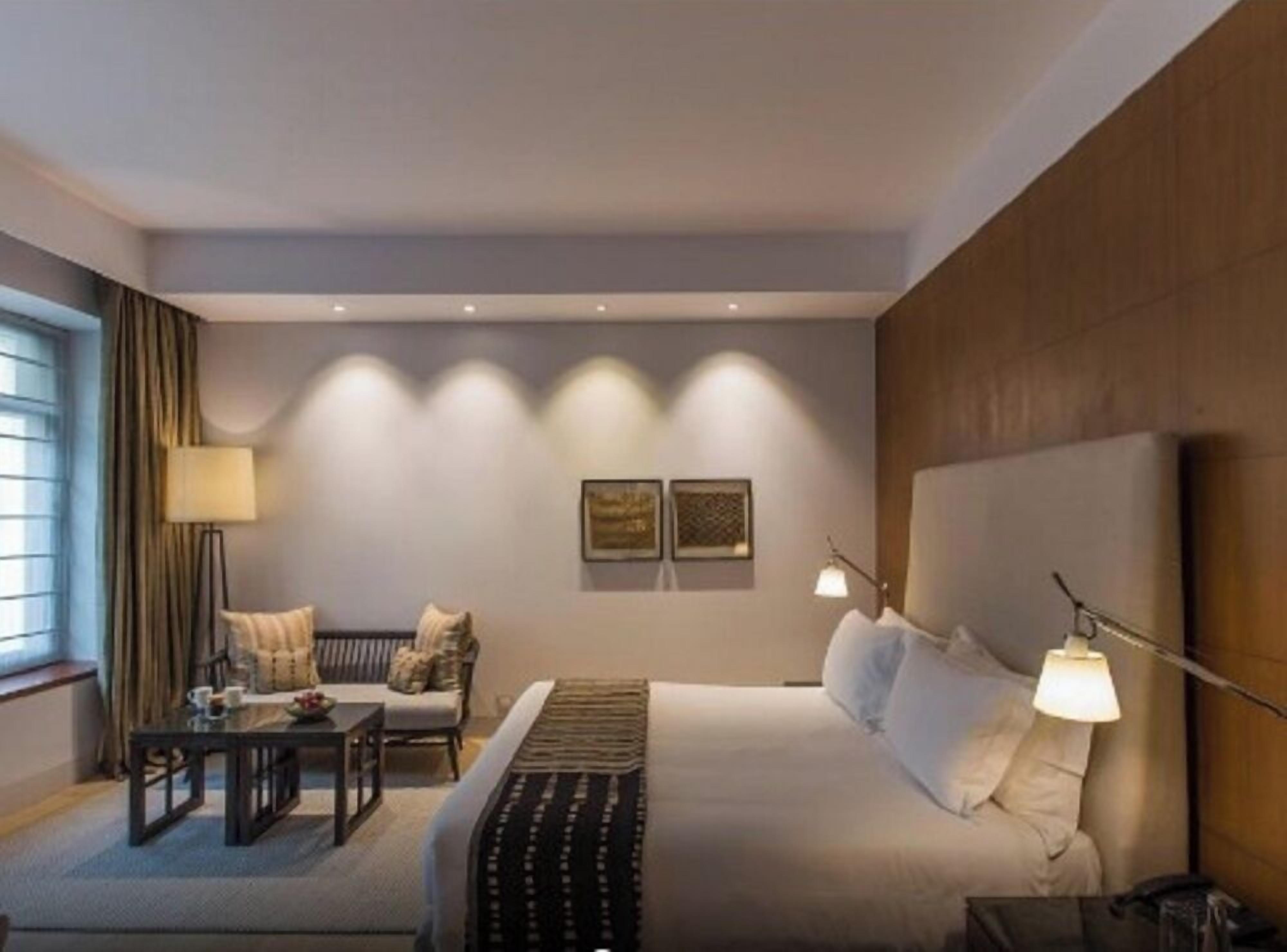 Quarto de hotel com cama, abajures, uma mesinha, um sofá e duas molduras de quadros penduradas na parede.
