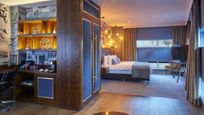 Quarto de hotel moderno com uma escrivaninha de madeira, uma cama, um espaço de estar e uma janela grande.