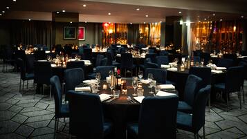 Restaurante com várias mesas montadas para refeições, com cadeiras azul-escuro e um chão estampado.