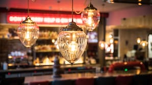 Uma área de bar com luminárias de vidro penduradas e um fundo desfocado com um letreiro vermelho.