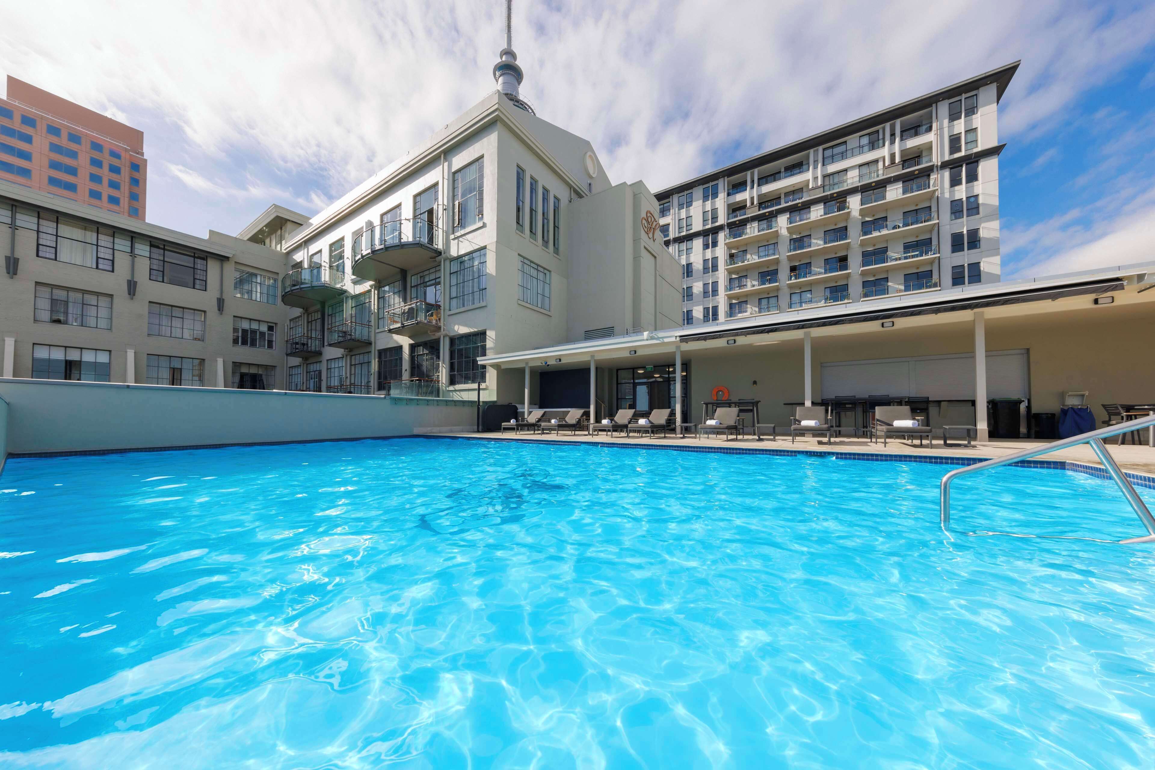 Piscina com espreguiçadeiras e área coberta, cercada por edifícios modernos.