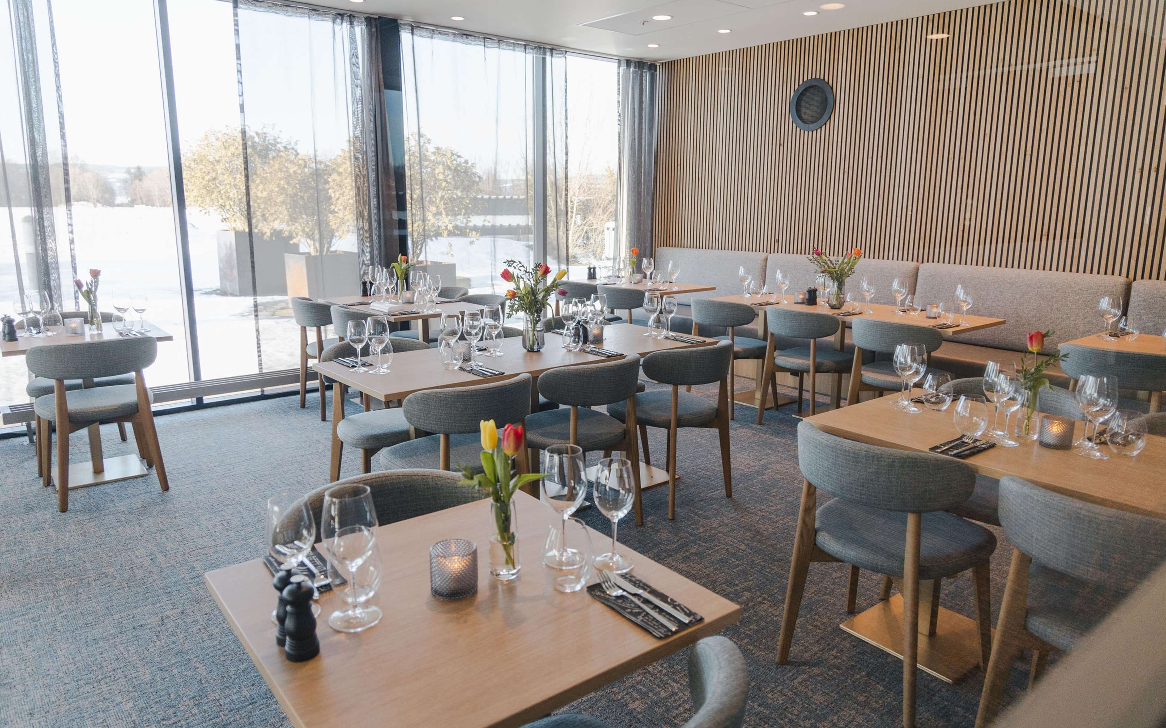 Restaurante moderno com mesas preparadas para refeições, grandes janelas e vista para o exterior.