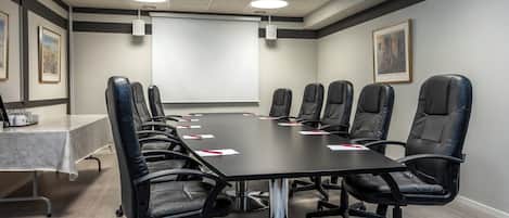 Uma sala de conferências com uma mesa comprida, cadeiras de couro preto, um projetor e uma lousa.