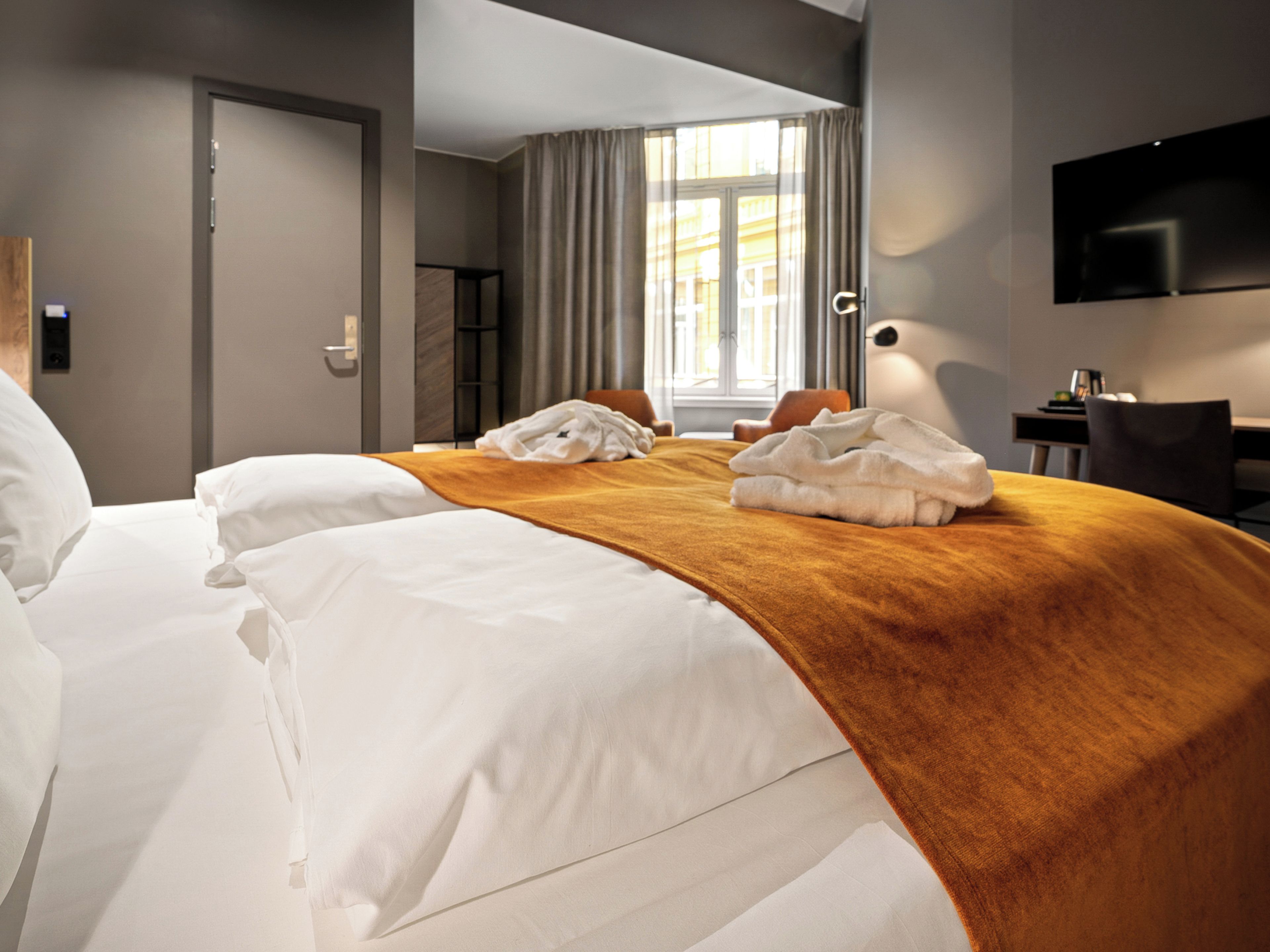 Quarto de hotel com uma cama grande, televisão e janela com cortinas.