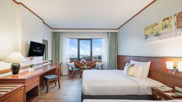 Quarto de hotel com cama, escrivaninha, cadeira, televisão e janela com vista.