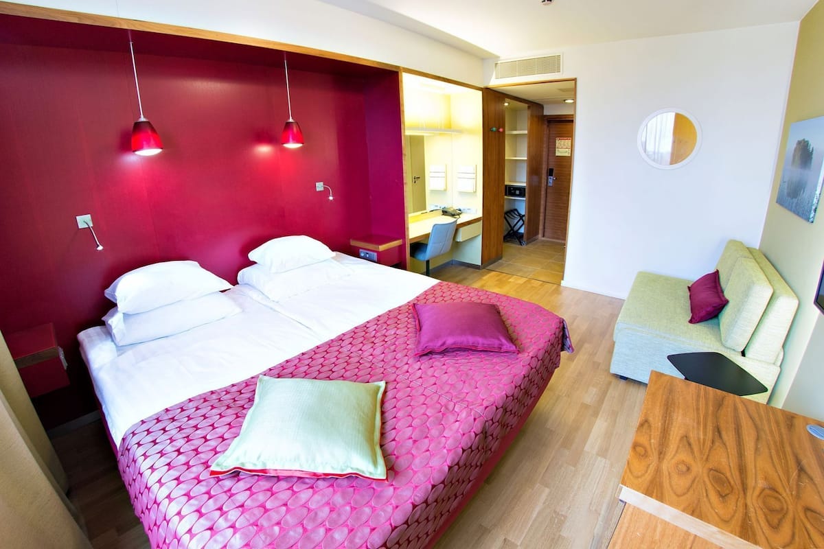 Quarto de hotel com cama, escrivaninha, cadeira e sofá.