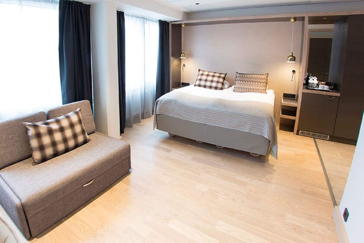 Quarto de hotel moderno com sofá, cama e cozinha compacta.