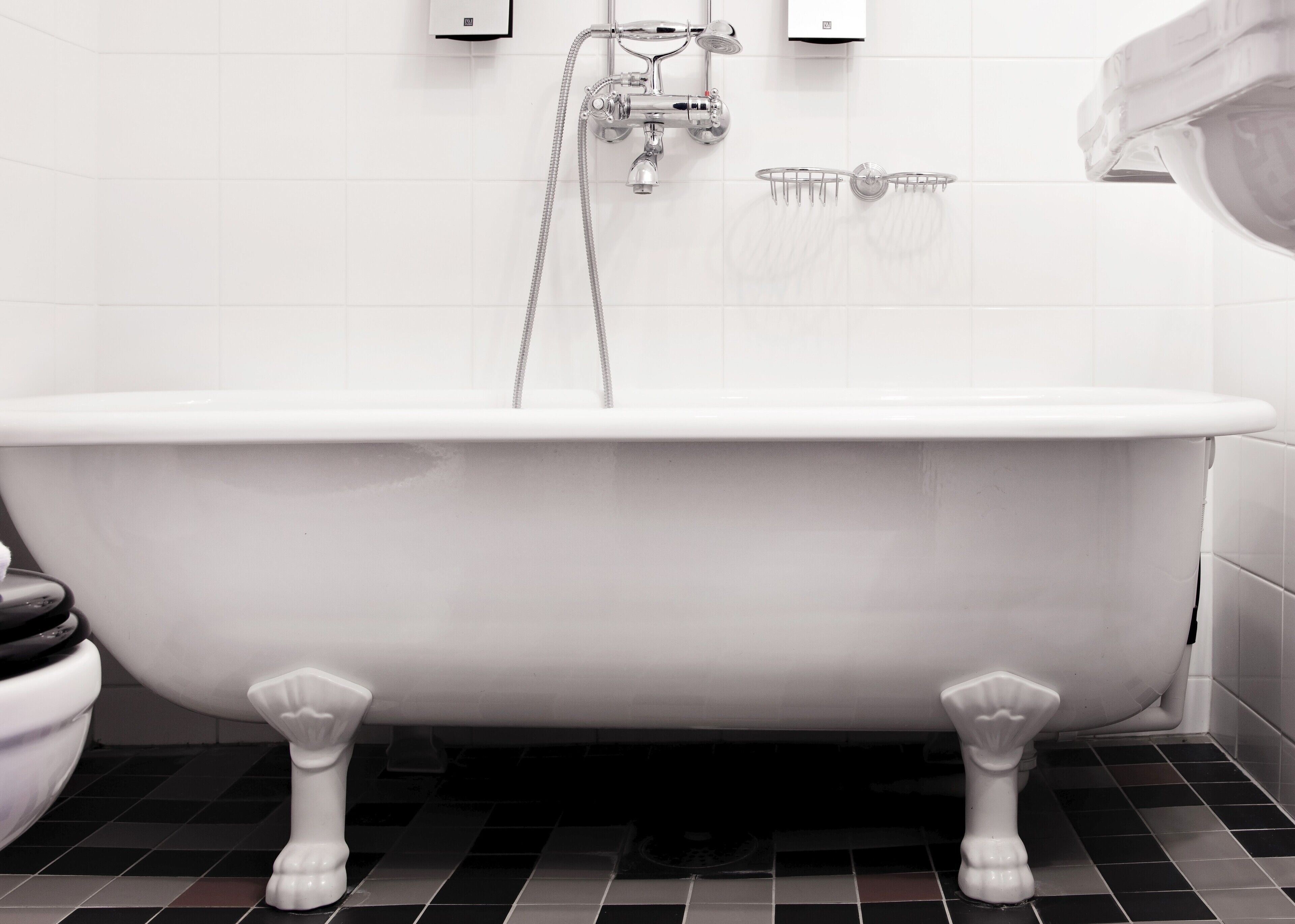 Uma banheira de pés de leão branca com chuveiro e mangueira, em frente a uma parede revestida de azulejos.