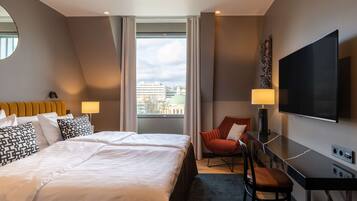 Quarto de hotel com uma cama grande, uma escrivaninha com televisão e vista para a cidade pela janela.