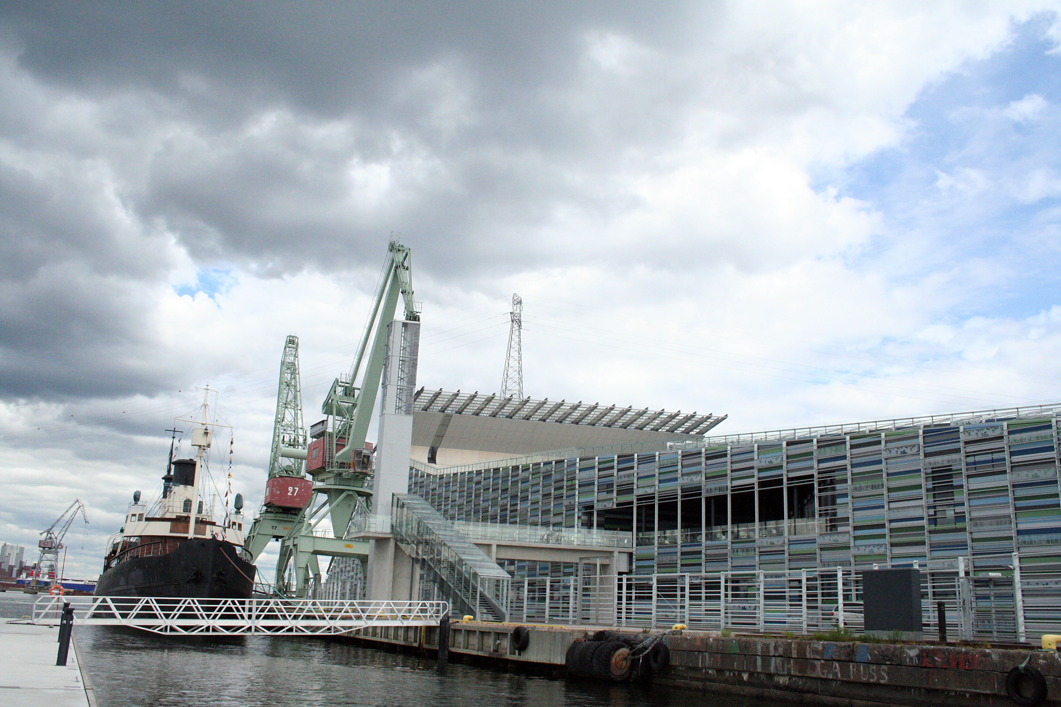Um grande edifício industrial com uma grua e um navio atracado nas proximidades.