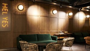 Uma sala de estar moderna com um sofá verde, poltronas florais e uma parede de madeira com luminárias circulares.