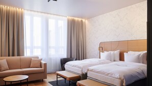 Quarto de hotel com sofá, duas camas, uma mesinha e uma cadeira.
