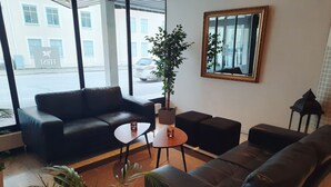 Uma sala de estar moderna com um sofá de couro preto, uma mesa redonda pequena e uma planta em vaso.