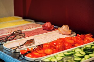 Buffet com diversos alimentos, incluindo carnes fatiadas, tomates e pepinos.