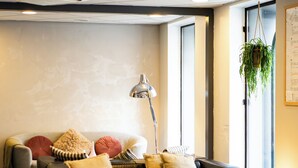 Uma sala de estar moderna com um sofá seccional, duas mesinhas laterais e uma planta pendente.