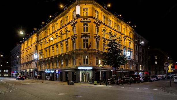 Um edifício histórico com entrada na esquina, várias janelas e uma placa indicando um hotel.