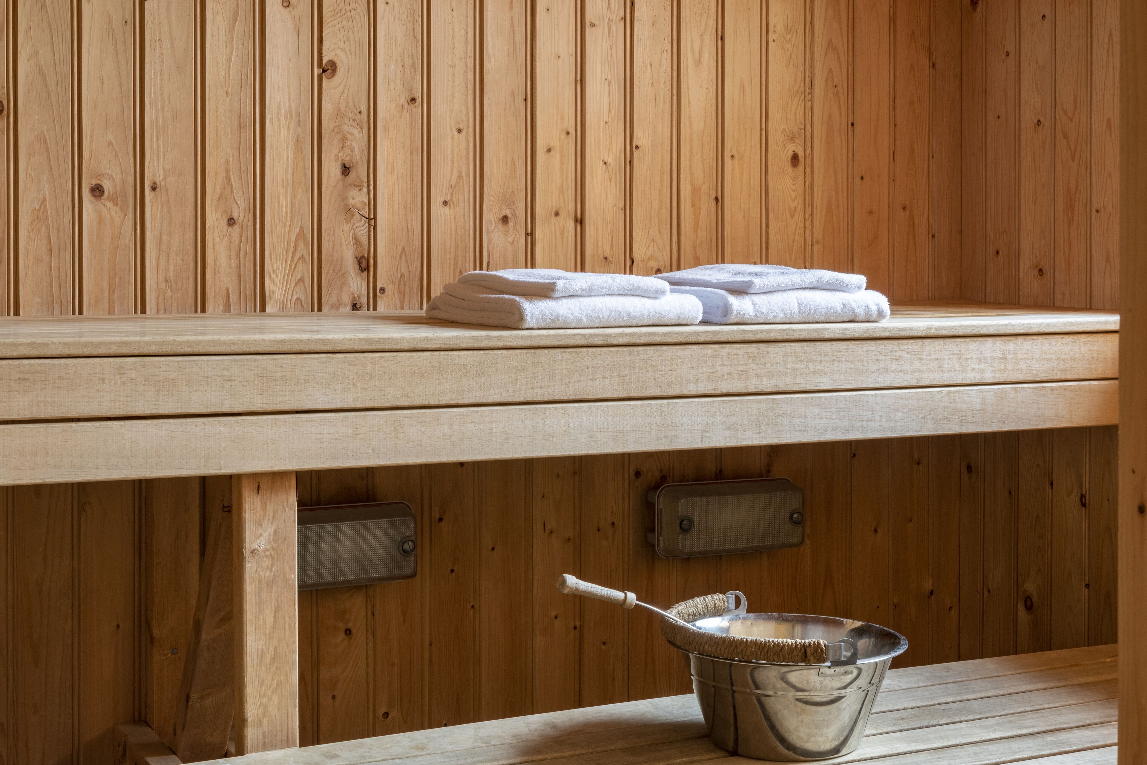 Uma sauna de madeira com um banco, toalhas e um balde de metal com uma escova.