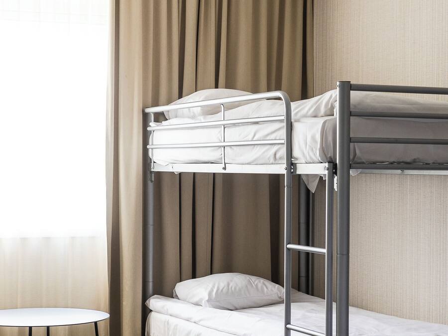 Uma cama beliche com escada, uma mesinha redonda e uma janela com cortinas.