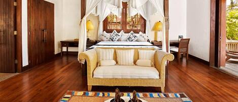 Quarto com cama de dossel, sofá, mesa de cabeceira e mesa com objetos decorativos.