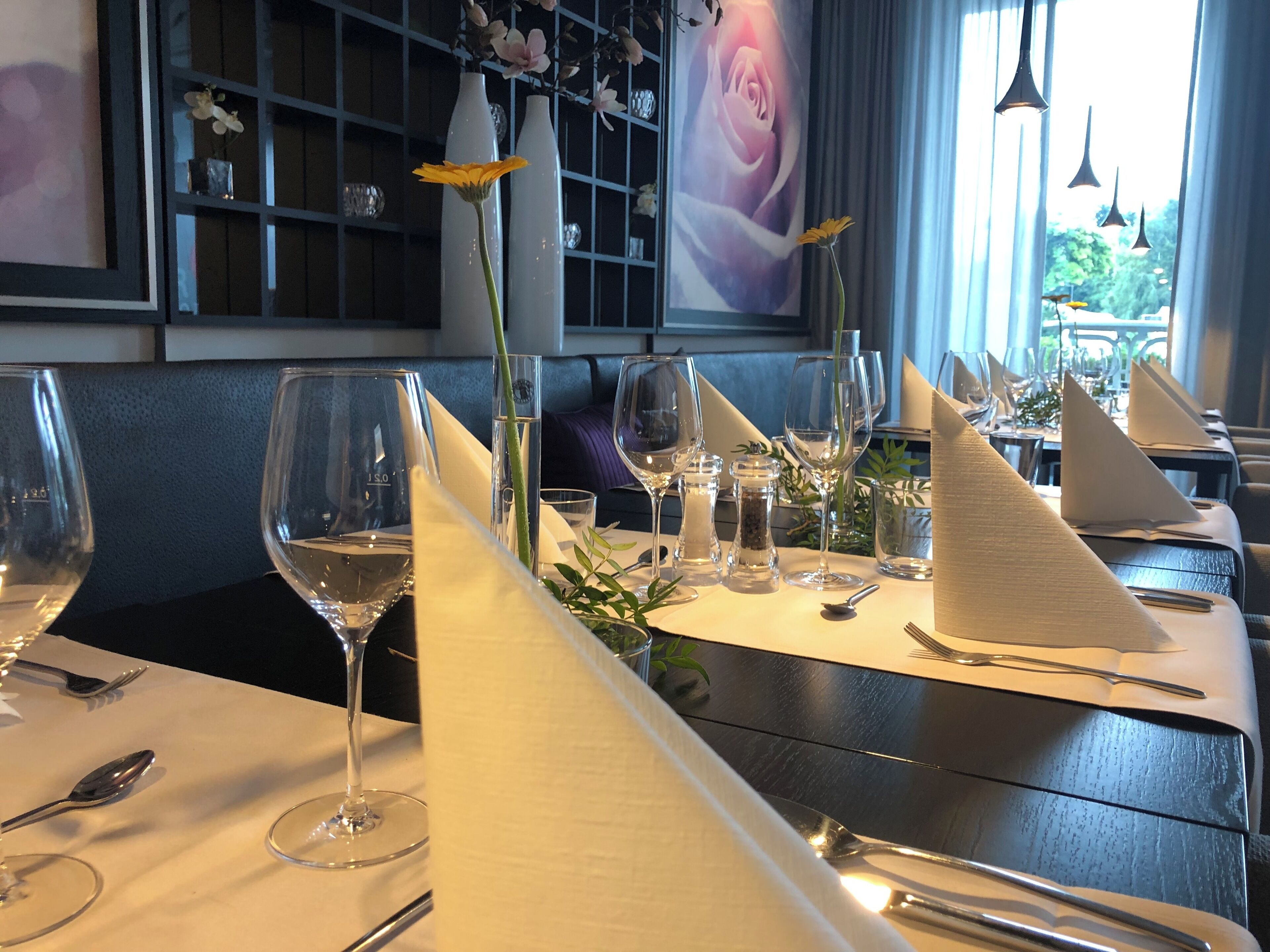 Mesa de restaurante posta com copos de vinho, copos de água e talheres.