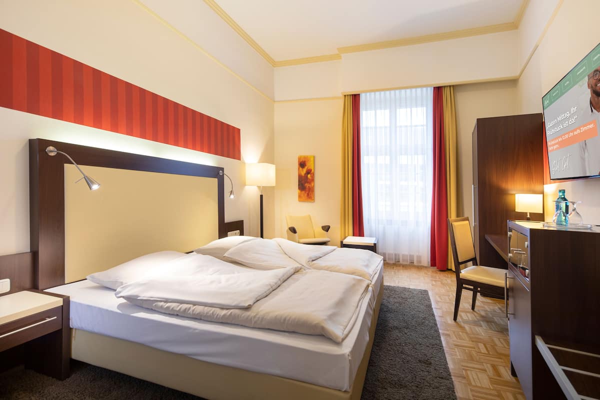 Quarto de hotel com uma cama grande, uma escrivaninha, uma cadeira e uma televisão exibindo uma mensagem.