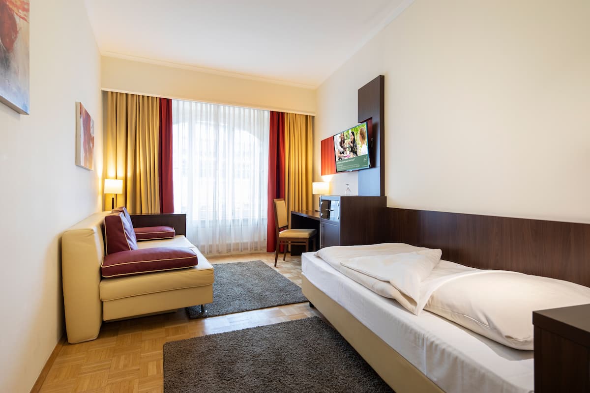 Quarto de hotel com cama, sofá, escrivaninha e televisão na parede.