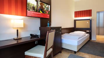 Quarto de hotel com cama, escrivaninha com luminária, poltrona, TV fixada na parede e minibar.