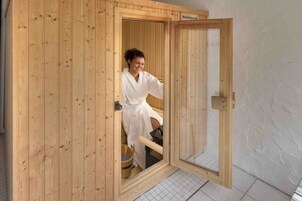 Uma sauna de madeira com porta deslizante, um banco de madeira no interior e um pequeno balde de madeira.