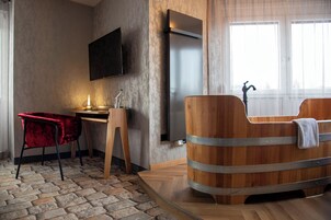Uma casa de banho moderna com uma banheira de madeira, uma cadeira vermelha, uma secretária de madeira e uma televisão montada na parede.