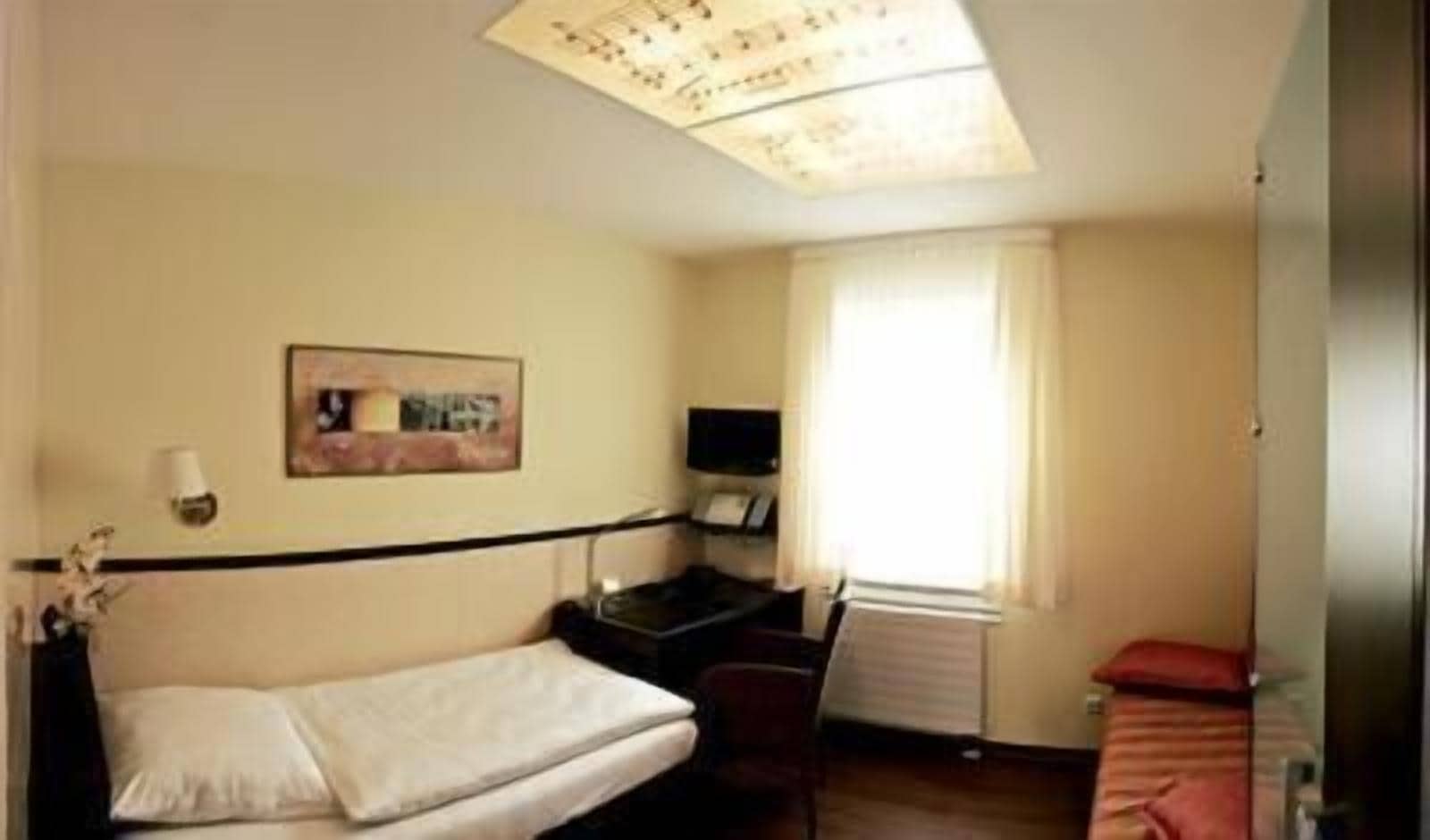 Quarto de hotel com cama, escrivaninha, cadeira, televisão e janela com cortinas.