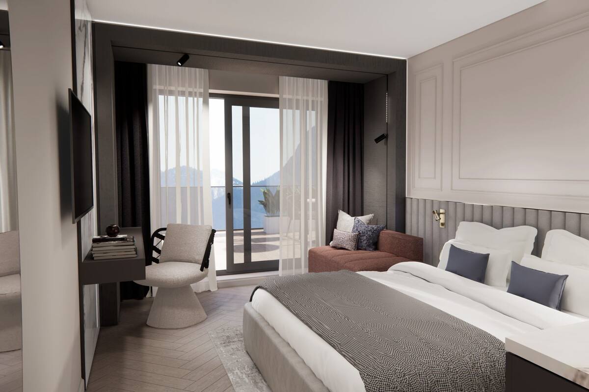 Quarto de hotel moderno com cama, sofá, poltrona e televisão.