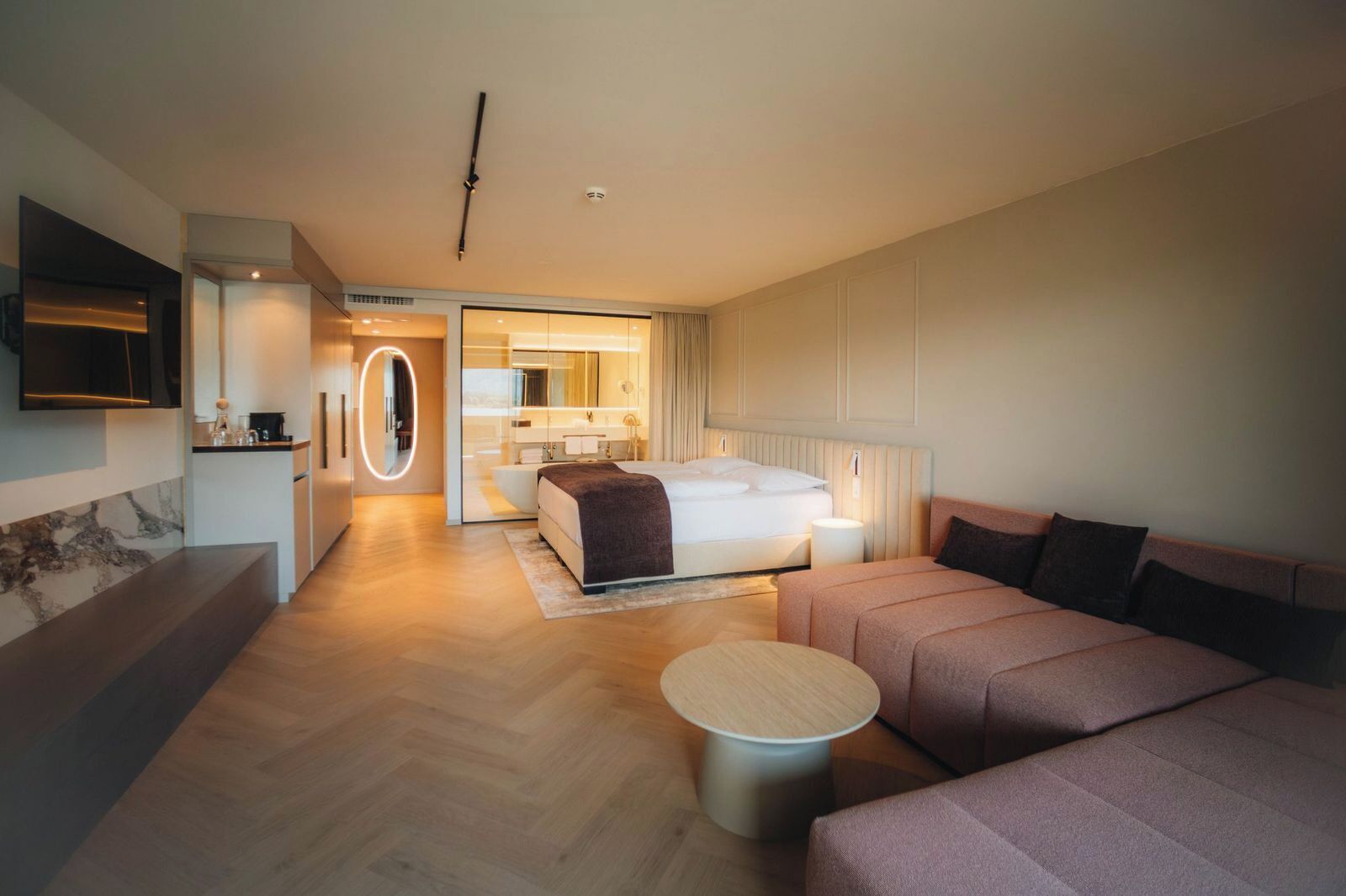 Quarto de hotel moderno com sofá, mesa redonda, cama e cozinha.