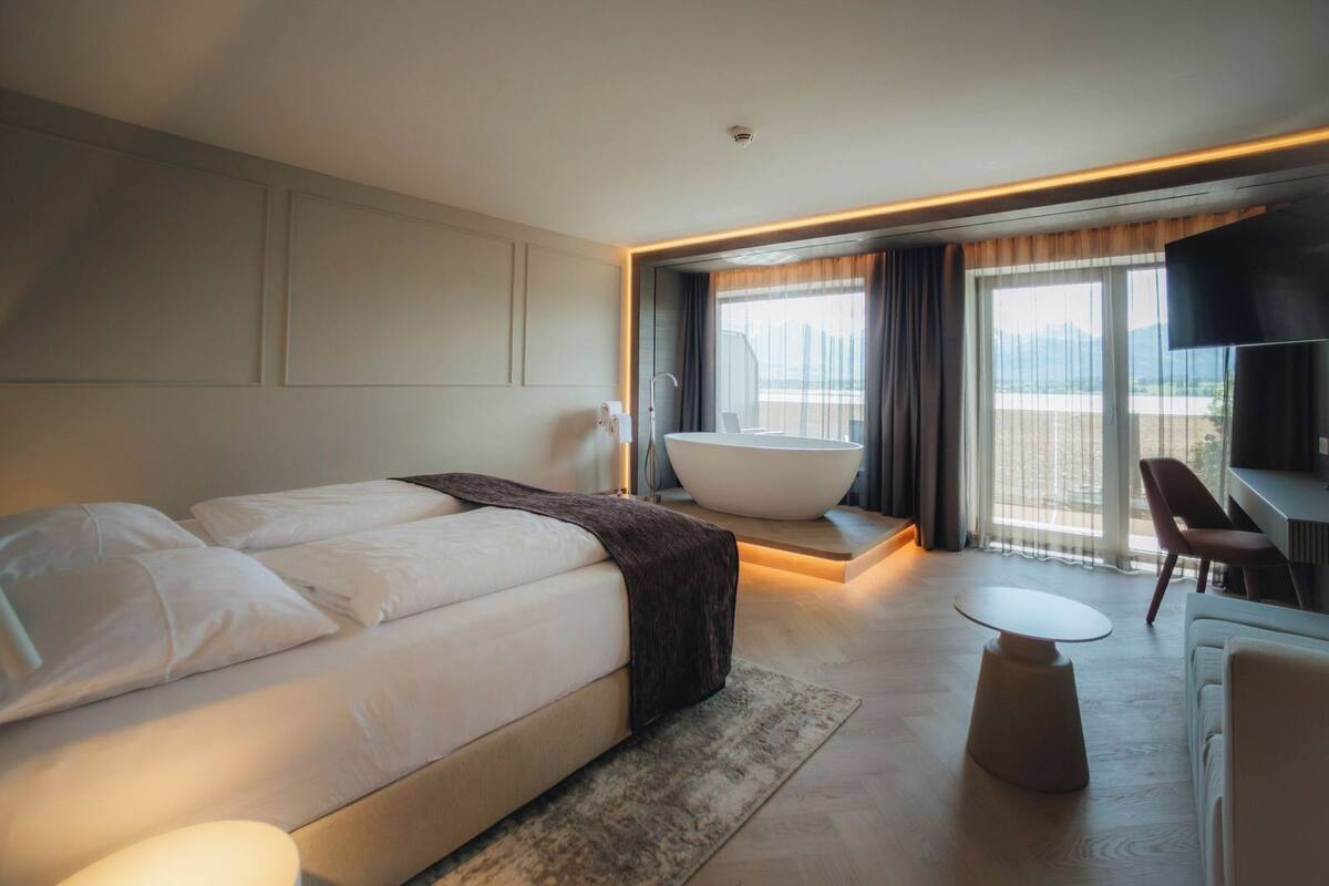 Quarto de hotel com uma cama grande, banheira, escrivaninha e televisão.