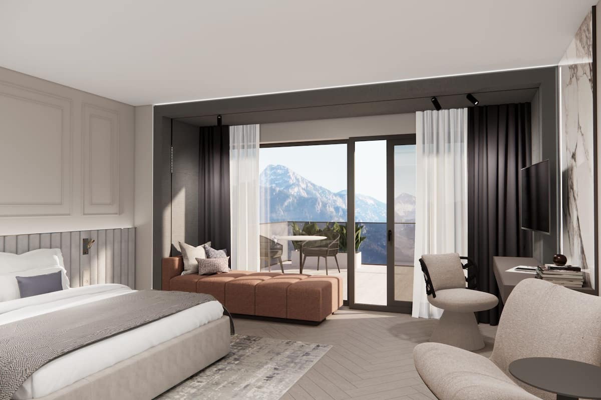 Quarto de hotel moderno com uma cama grande, um sofá, uma pequena mesa e uma cadeira. Há uma varanda com vista para as montanhas.