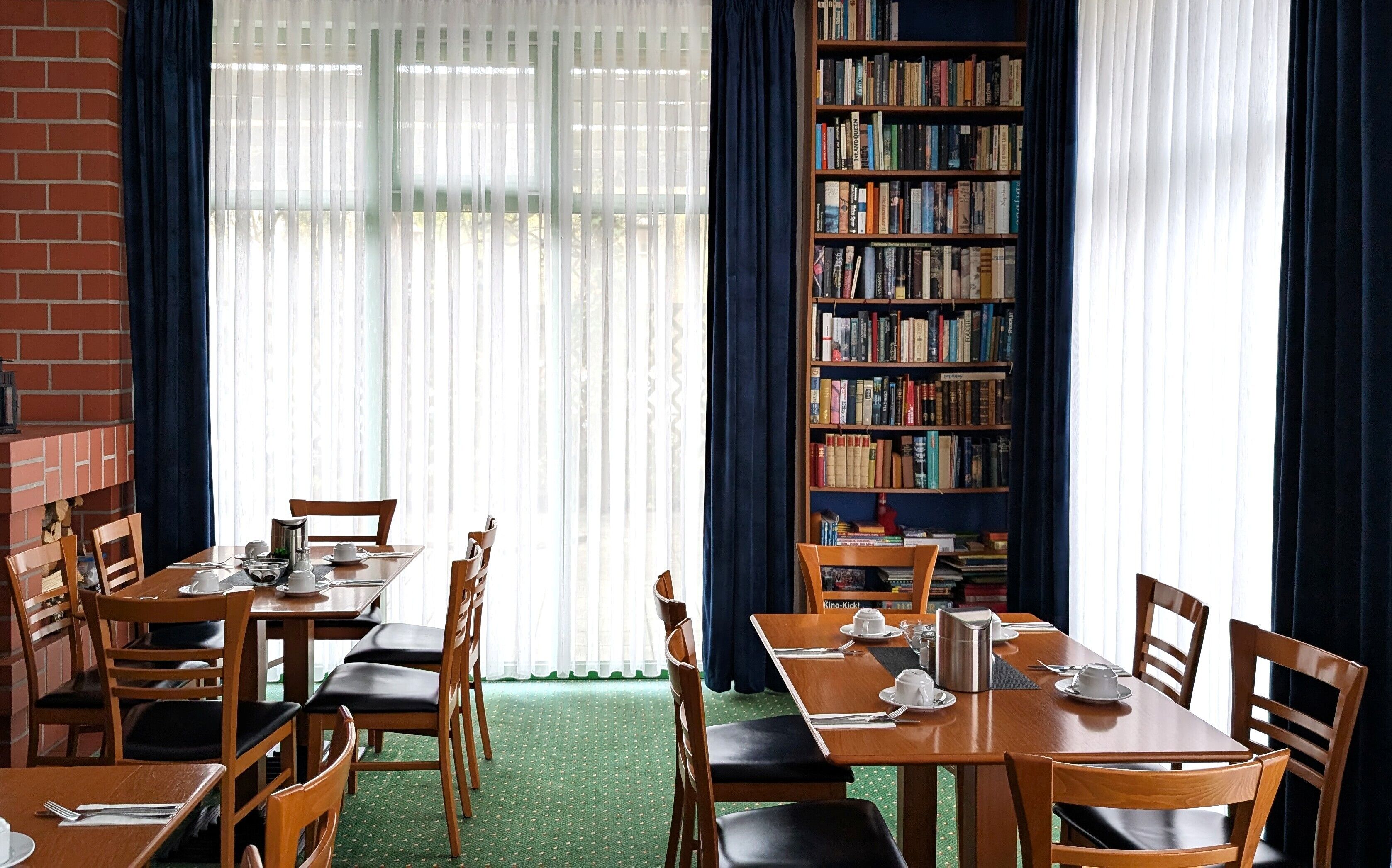 Uma área de refeições com parede de tijolos, uma estante cheia de livros e uma mesa posta para quatro cadeiras.
