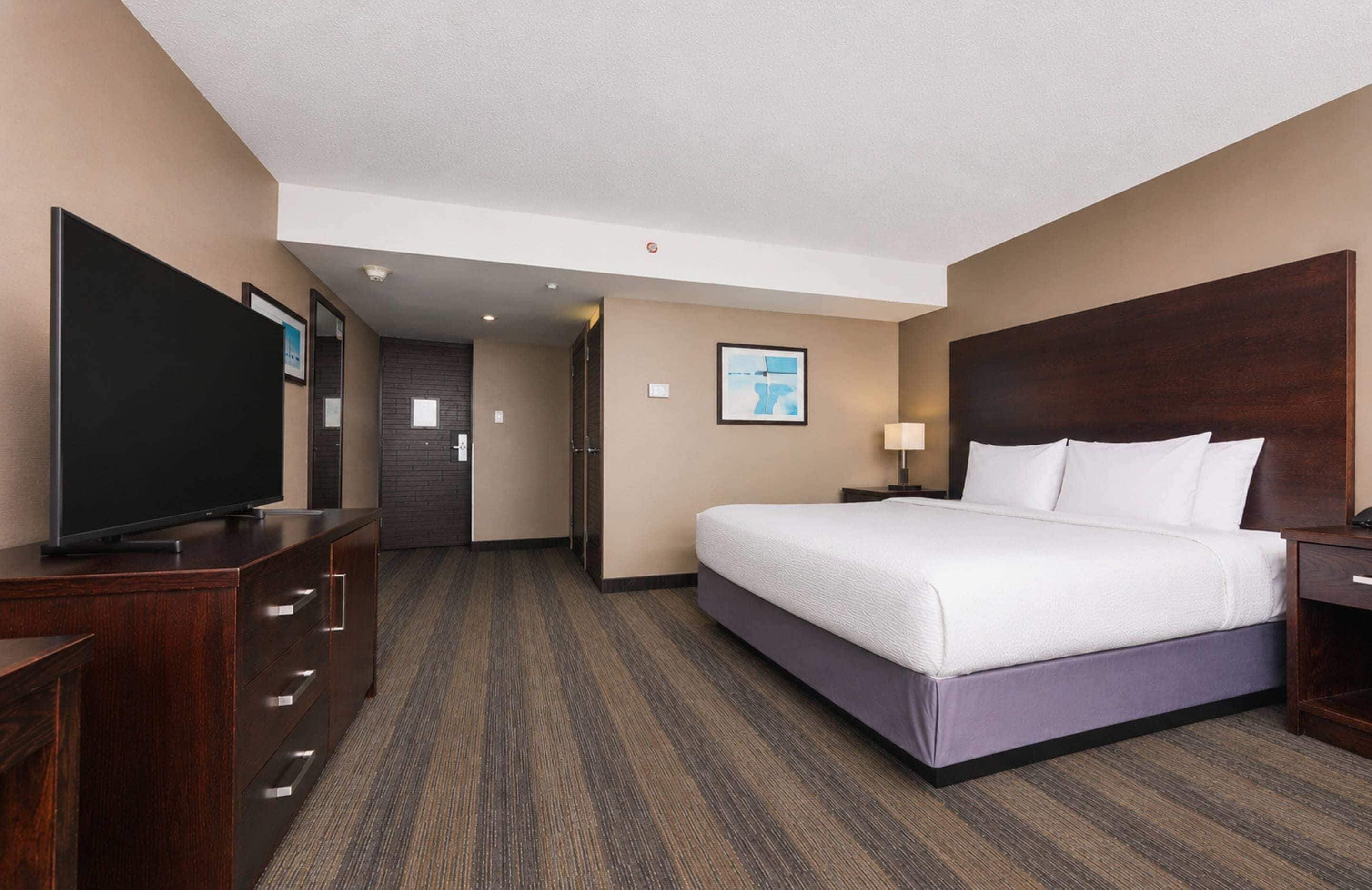 Quarto de hotel com cama, televisão, escrivaninha e guarda-roupa.