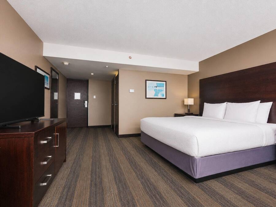 Quarto de hotel com cama, televisão, escrivaninha e guarda-roupa.