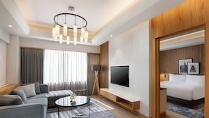 Quarto de hotel moderno com uma televisão de tela plana grande, um sofá, uma mesa de centro e uma cama.