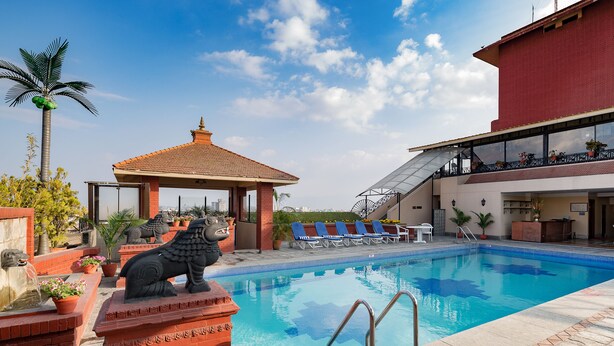 Uma piscina com uma estátua de leão de pedra, cadeiras de sol e uma área de estar coberta.