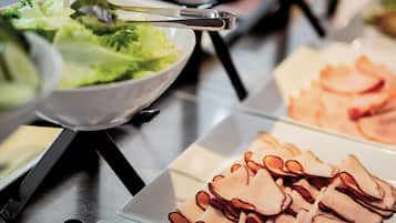 Buffet com diversos alimentos, incluindo carnes fatiadas, vegetais e saladas.