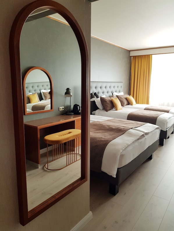 Quarto de hotel com um espelho grande, uma mesa com cadeira, duas camas e uma janela com cortinas.