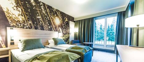 Quarto de hotel com uma janela ampla, cama, escrivaninha e um mural na parede.