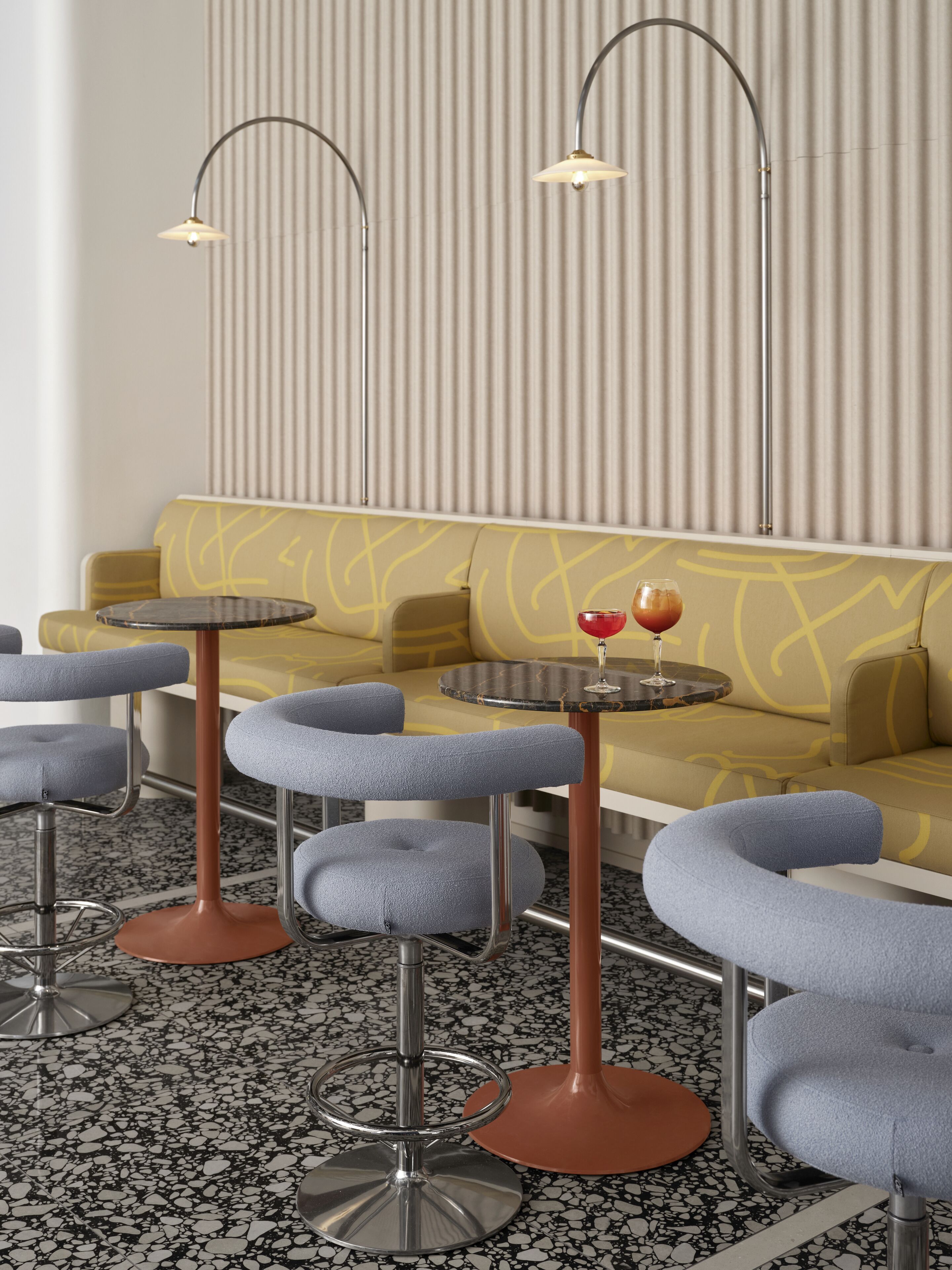 Uma área de estar moderna com um sofá, dois bancos altos para bar e uma mesinha com um copo e uma garrafa.