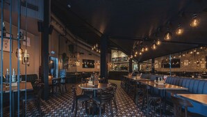 Um restaurante com piso estampado, mesas, cadeiras e lâmpadas penduradas.