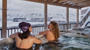 Uma cabana de madeira com hidromassagem e vista para montanhas cobertas de neve.