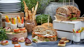 Diversos alimentos, incluindo sanduíches, aperitivos e bebidas, dispostos sobre uma mesa com fundo de madeira rústica.