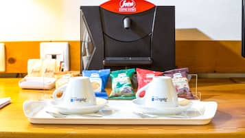 Uma estação de café com uma máquina de café, duas xícaras e diversos sachês de café em um suporte.