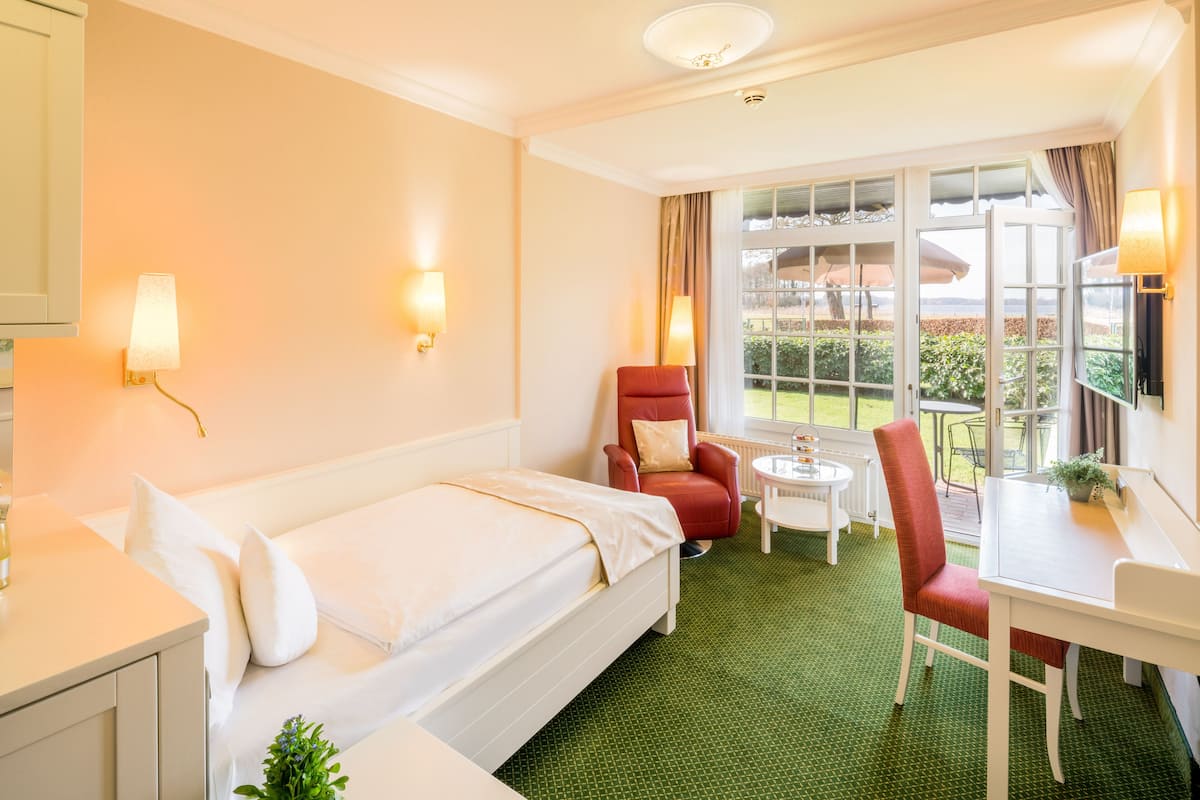 Quarto de hotel com uma cama, uma poltrona vermelha, uma mesinha e uma janela com vista para o exterior.